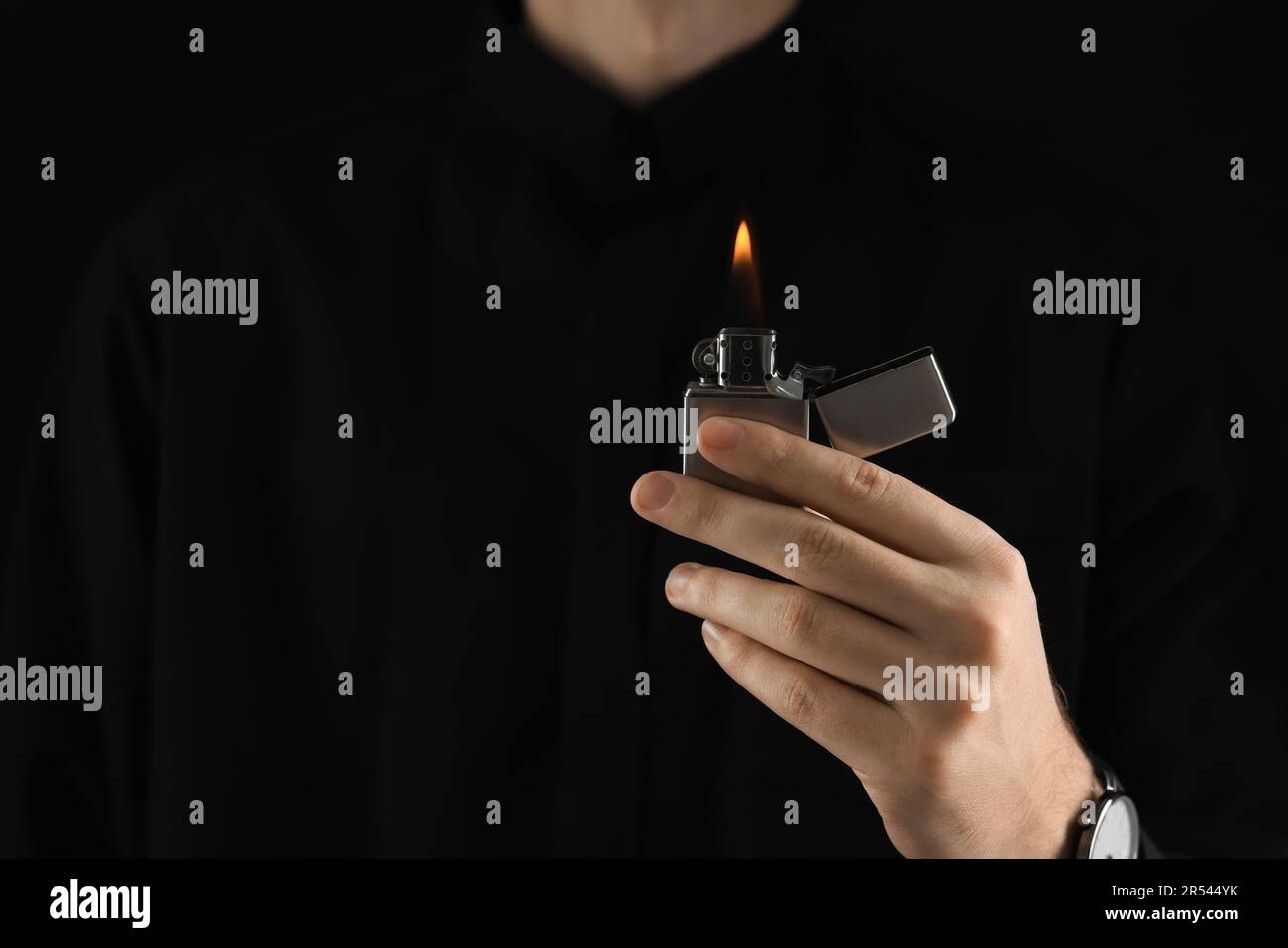 Man holding lighter with burning flame on black background, closeup ...
