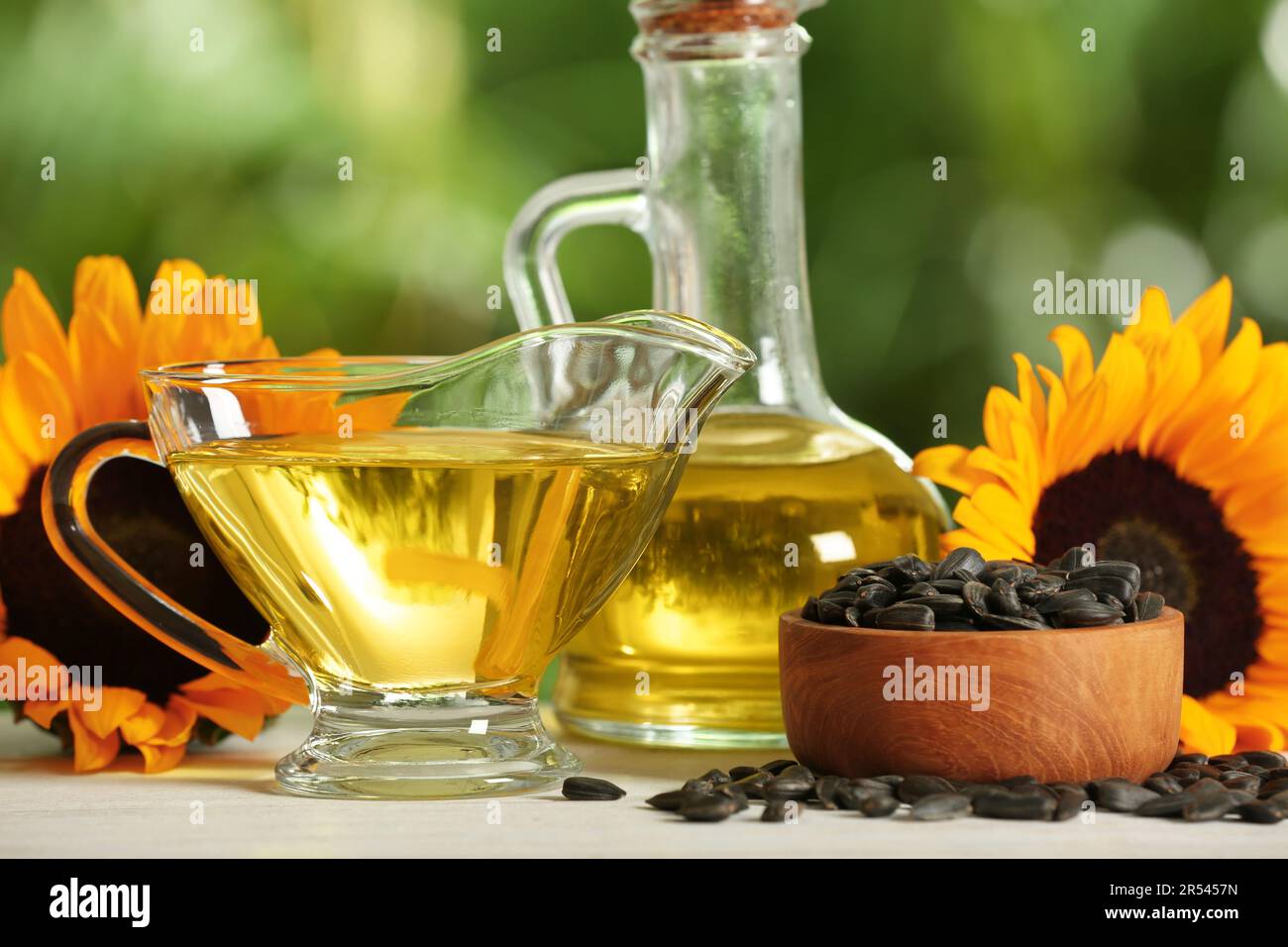 Sunflower cooking oil, seeds and yellow flowers on white wooden table ...
