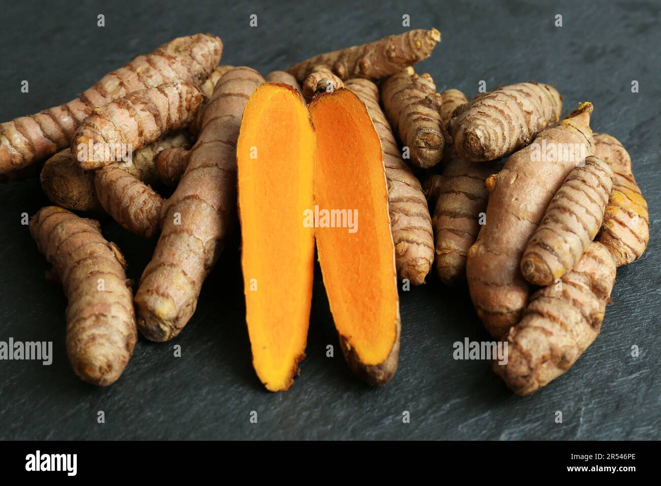 Whole and cut turmeric roots on black textured table, closeup Stock ...