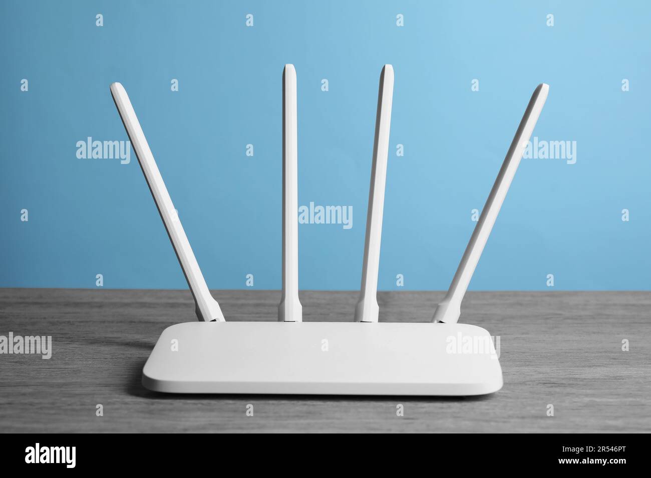 New white Wi-Fi router on wooden table against light blue background ...