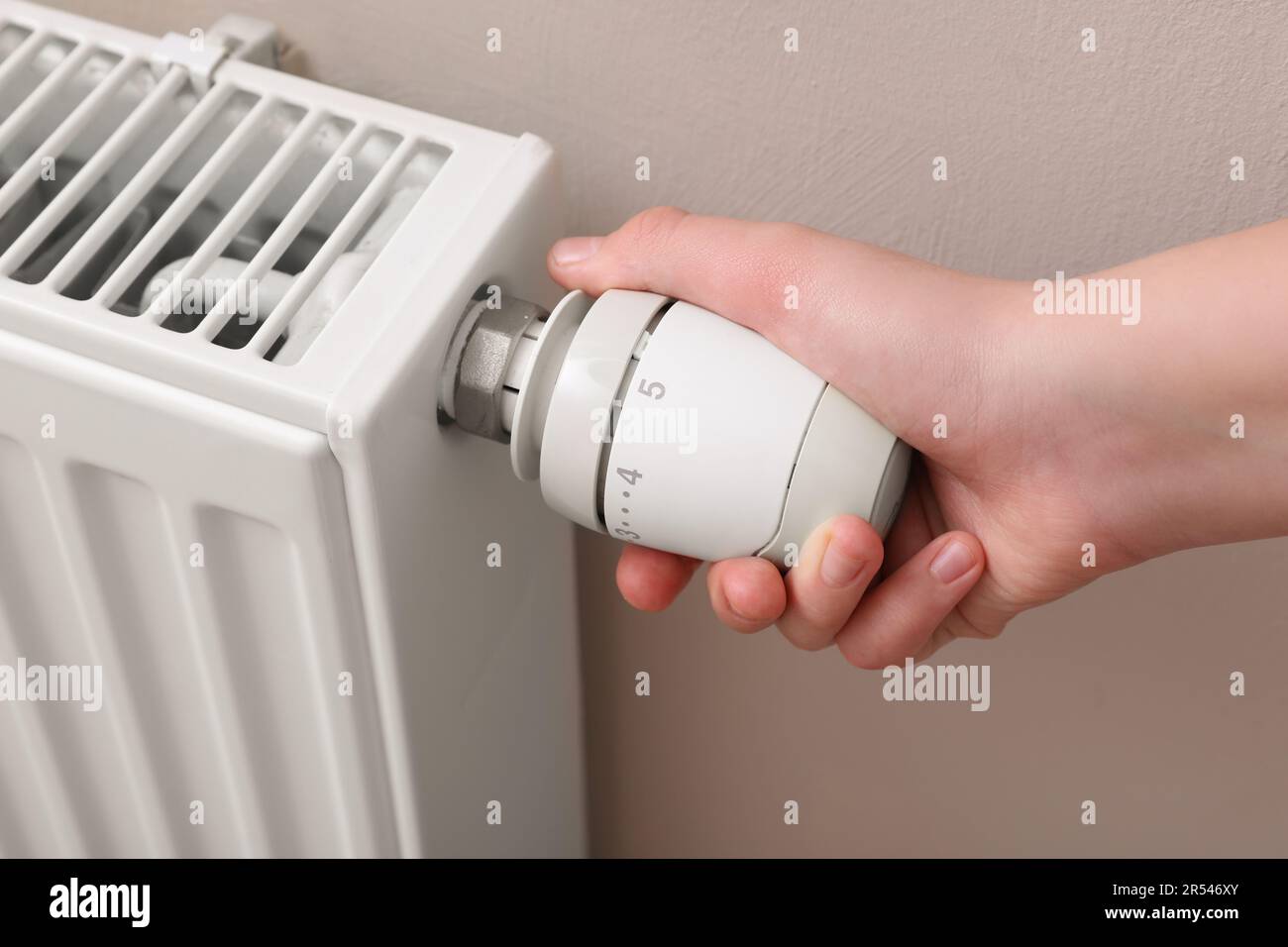 Girl adjusting heating radiator thermostat near white wall, closeup ...