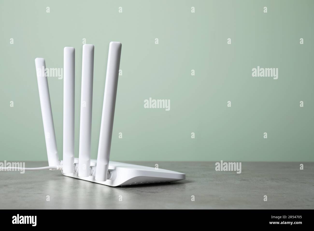 New modern Wi-Fi router on grey table near green wall, space for text ...