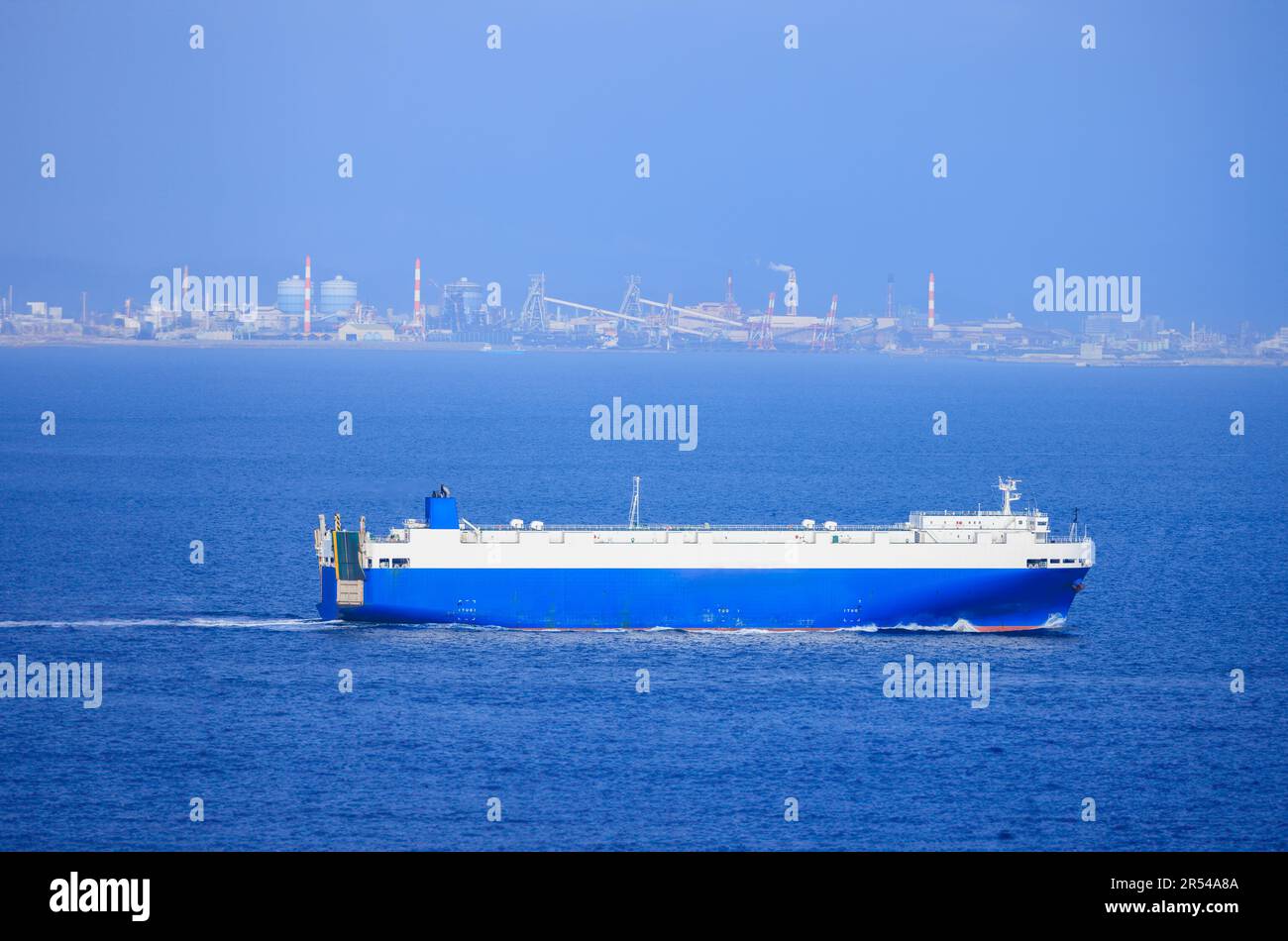 Cargo ship sails past smokestacks at industrial refinery on coast Stock ...