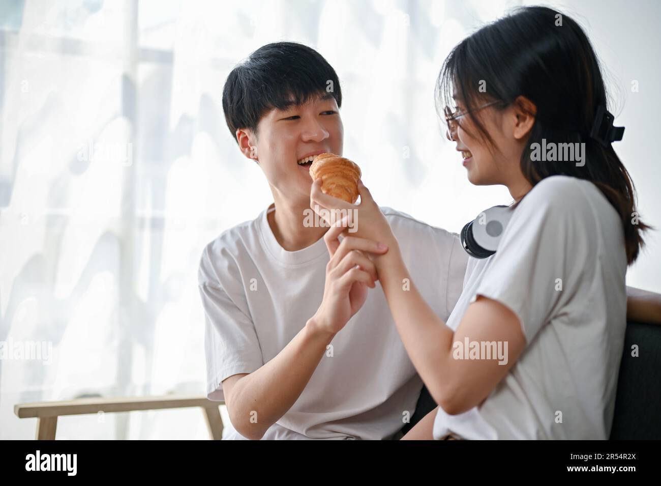 A cute girlfriend feeds a croissant to her boyfriend. A lovely young ...