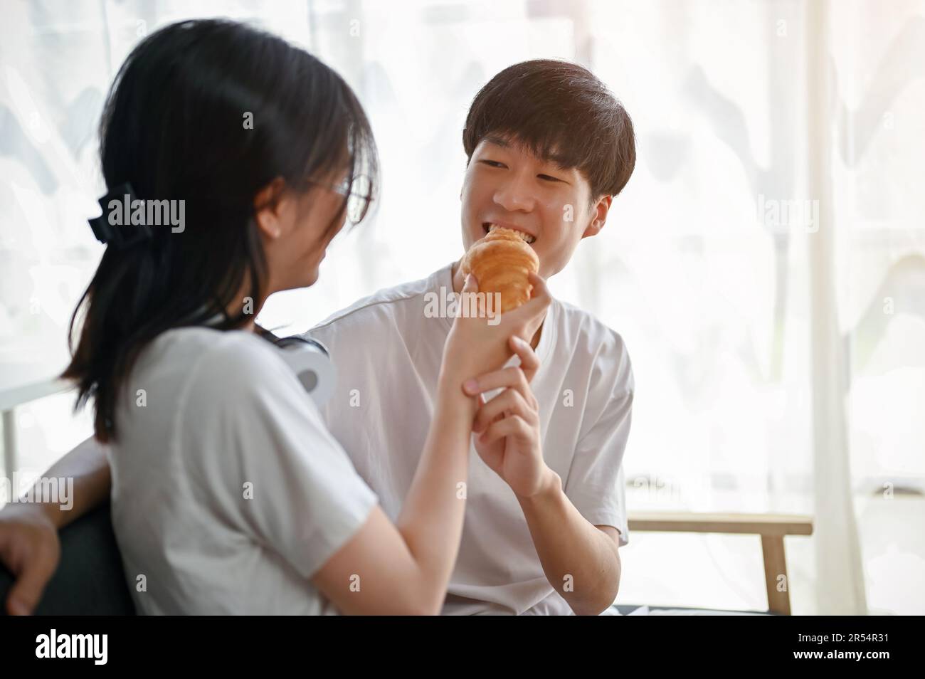 A cute girlfriend feeds a croissant to her boyfriend. A lovely young ...