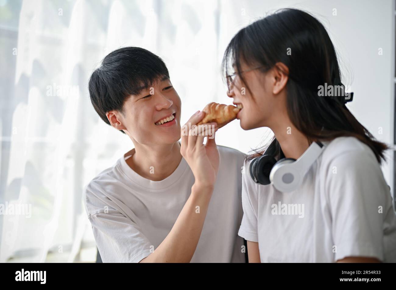 A cute young Asian boyfriend feeds a croissant to his girlfriend. A ...