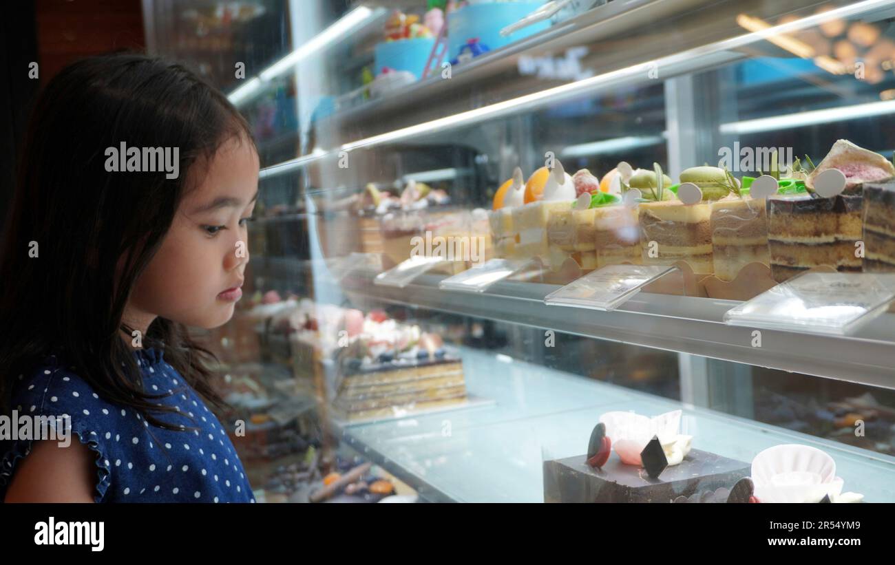 Asian little girl looking at cakes and sweets on display in a bakery ...