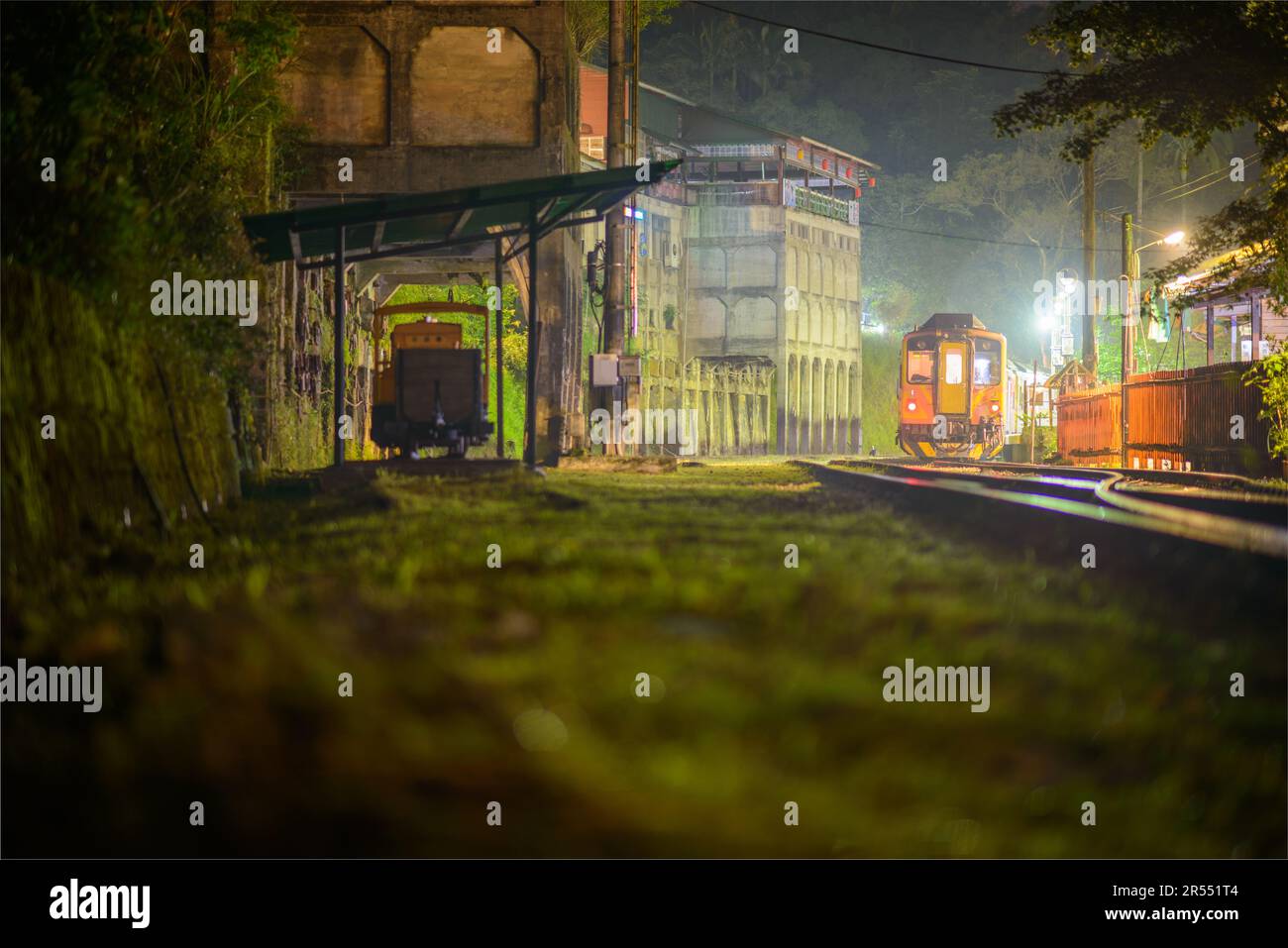 A yellow diesel train pulls into the station at night with lights on ...