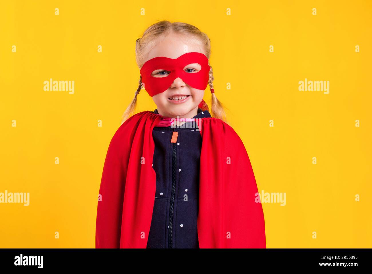 Funny little power superhero child girl in a red raincoat and a mask ...