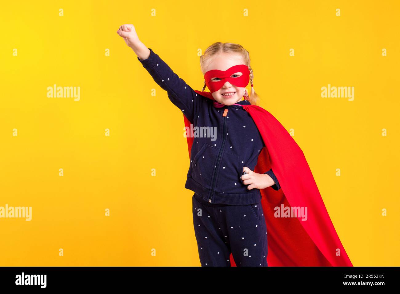 Funny little power superhero child girl in a red raincoat and a mask ...