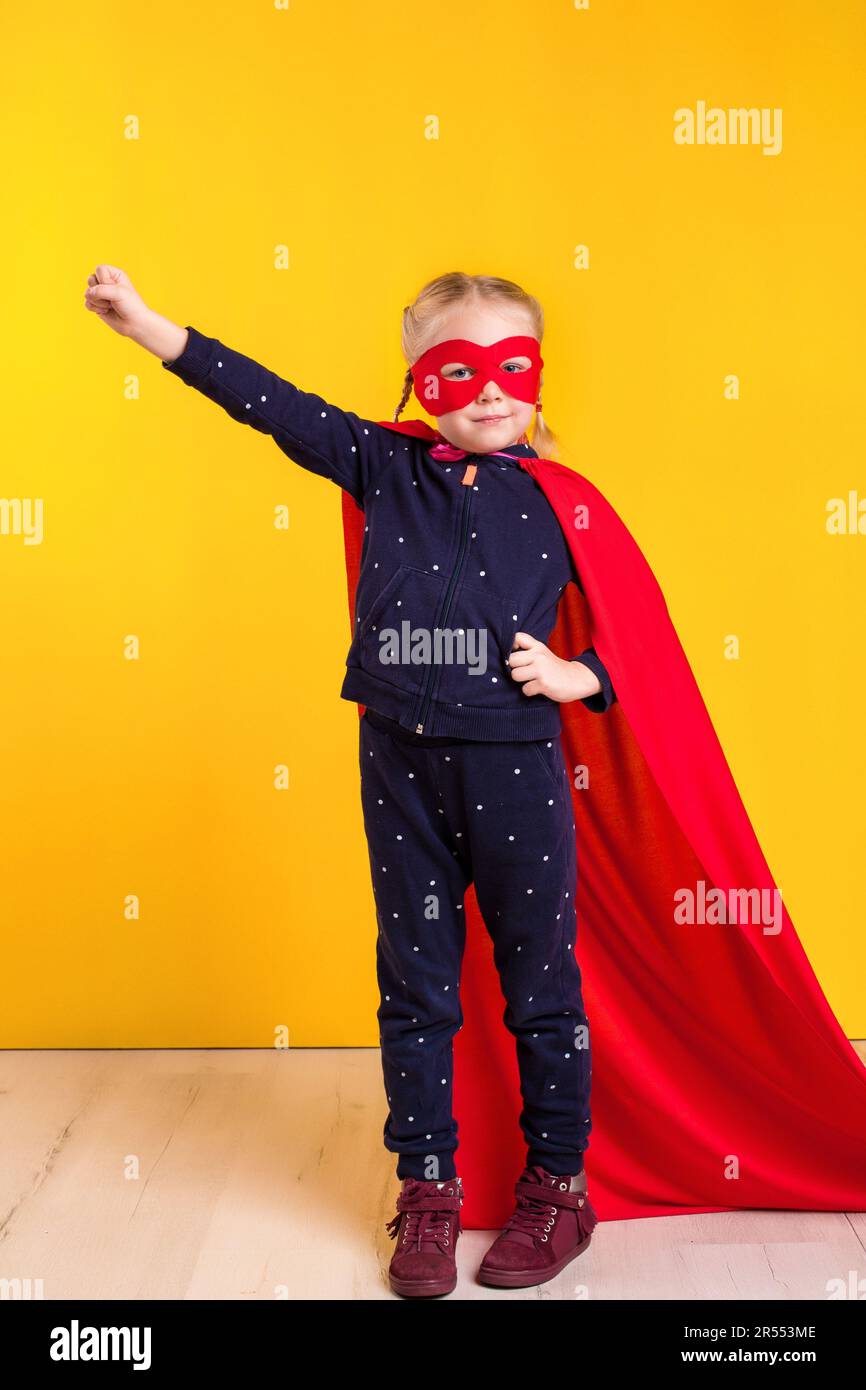Funny little power superhero child girl in a red raincoat and a mask ...