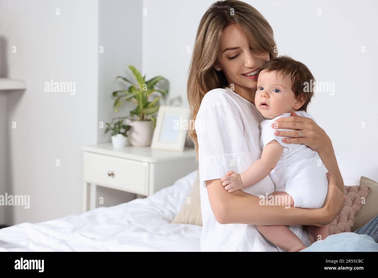 Mother hugging her cute little baby in bedroom, space for text Stock ...