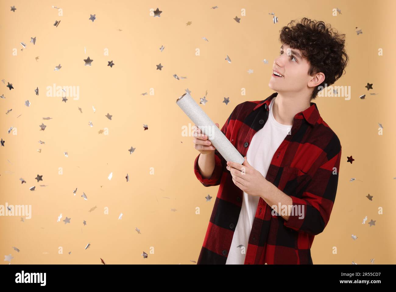 Happy teenage boy blowing up party popper on light brown background ...