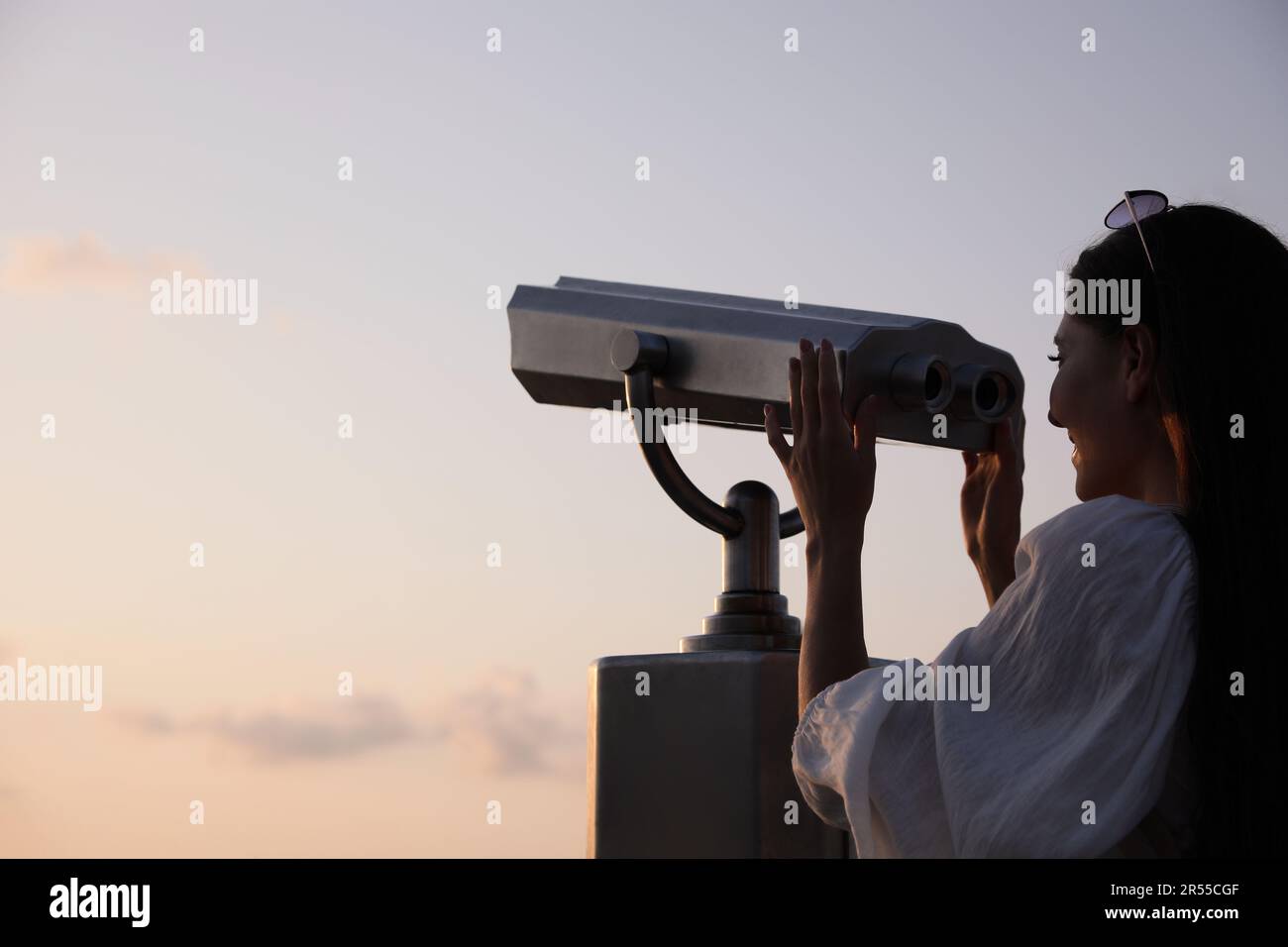 Young woman looking through tourist viewing machine at observation deck ...