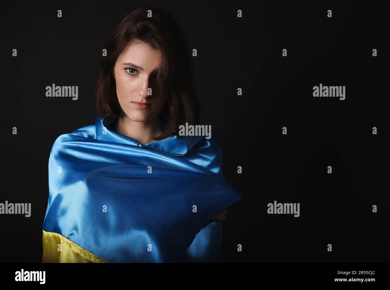 Sad woman wrapped in Ukrainian flag on black background. Space for text ...