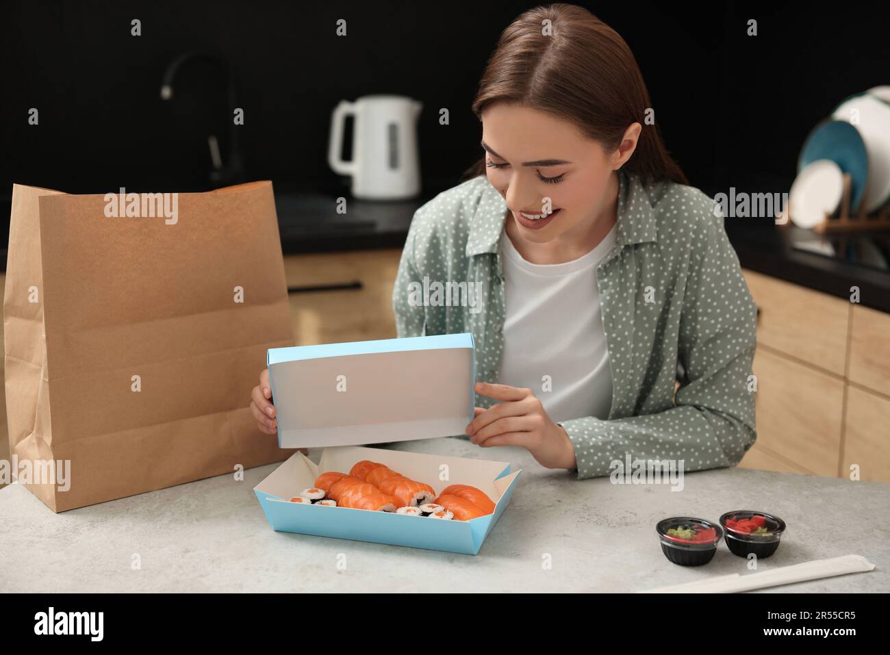 Beautiful young woman unpacking her order from sushi restaurant at ...