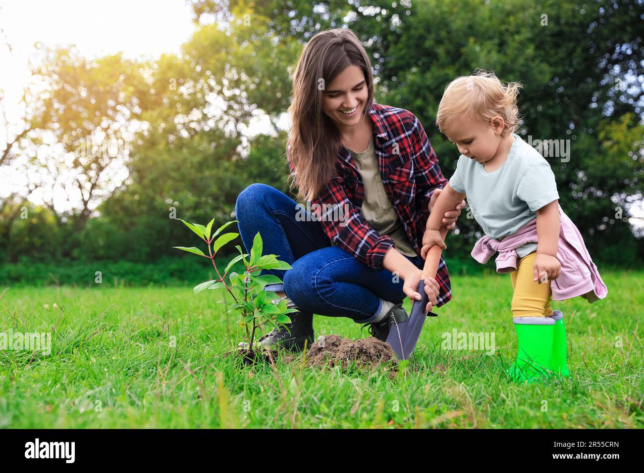 Mother and her baby daughter planting tree together in garden Stock ...