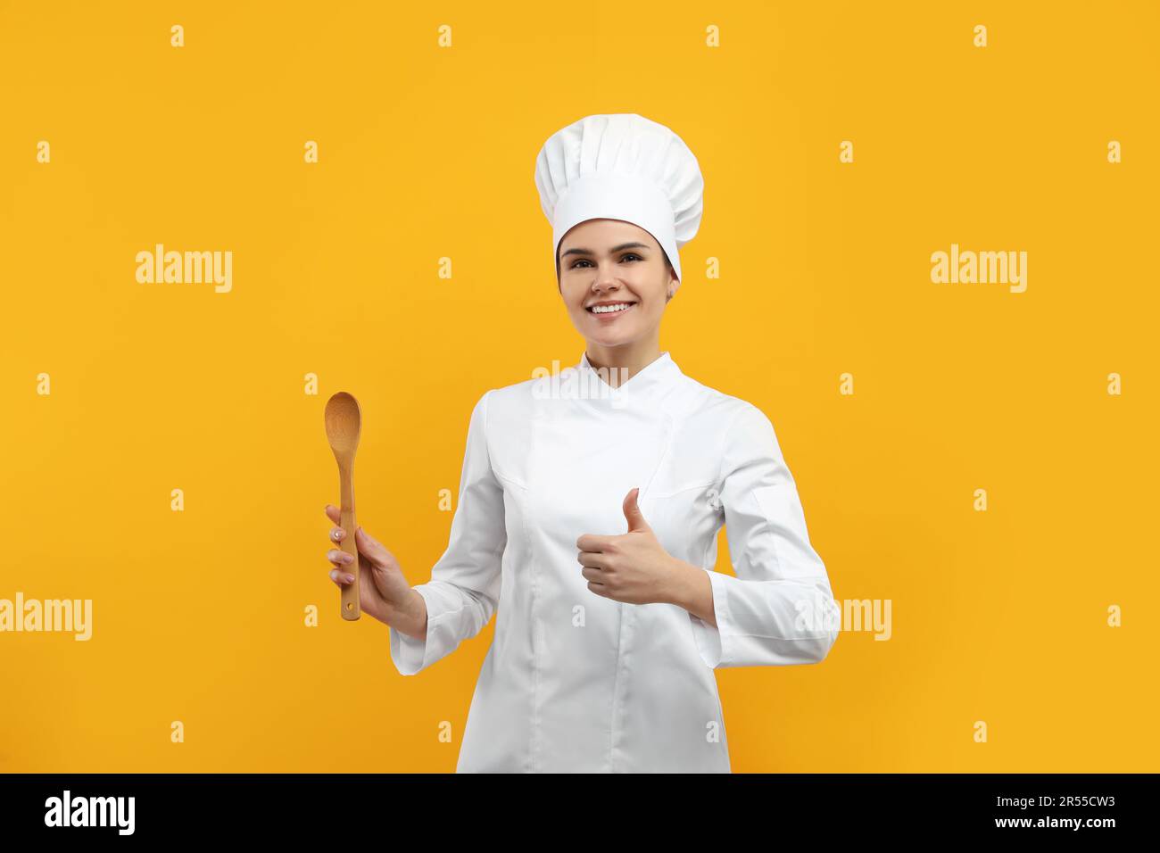 Happy chef with wooden spoon showing thumbs up on orange background ...