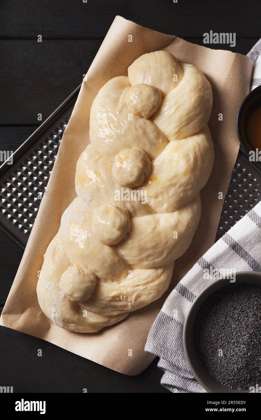 Raw braided bread and poppy seeds on black wooden table, flat lay ...