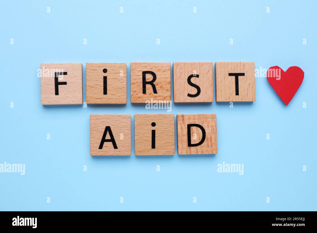 Words First Aid made of wooden cubes and cardboard heart on light blue ...