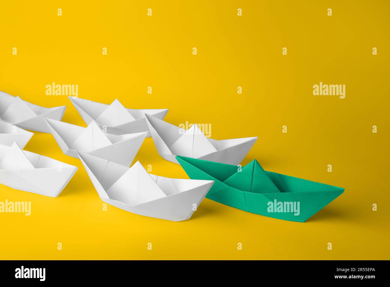 Group of paper boats following green one on yellow background ...