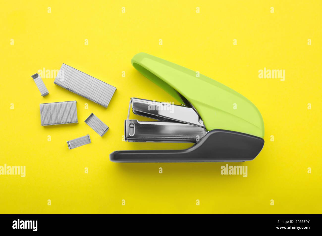 New bright stapler with staples on yellow background, fat lay. School ...