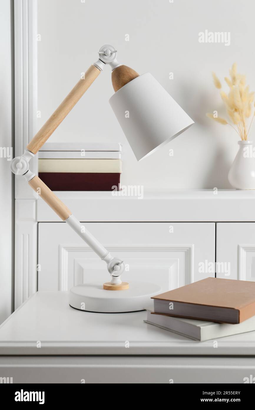 Stylish lamp and books on white side table in light room. Interior ...
