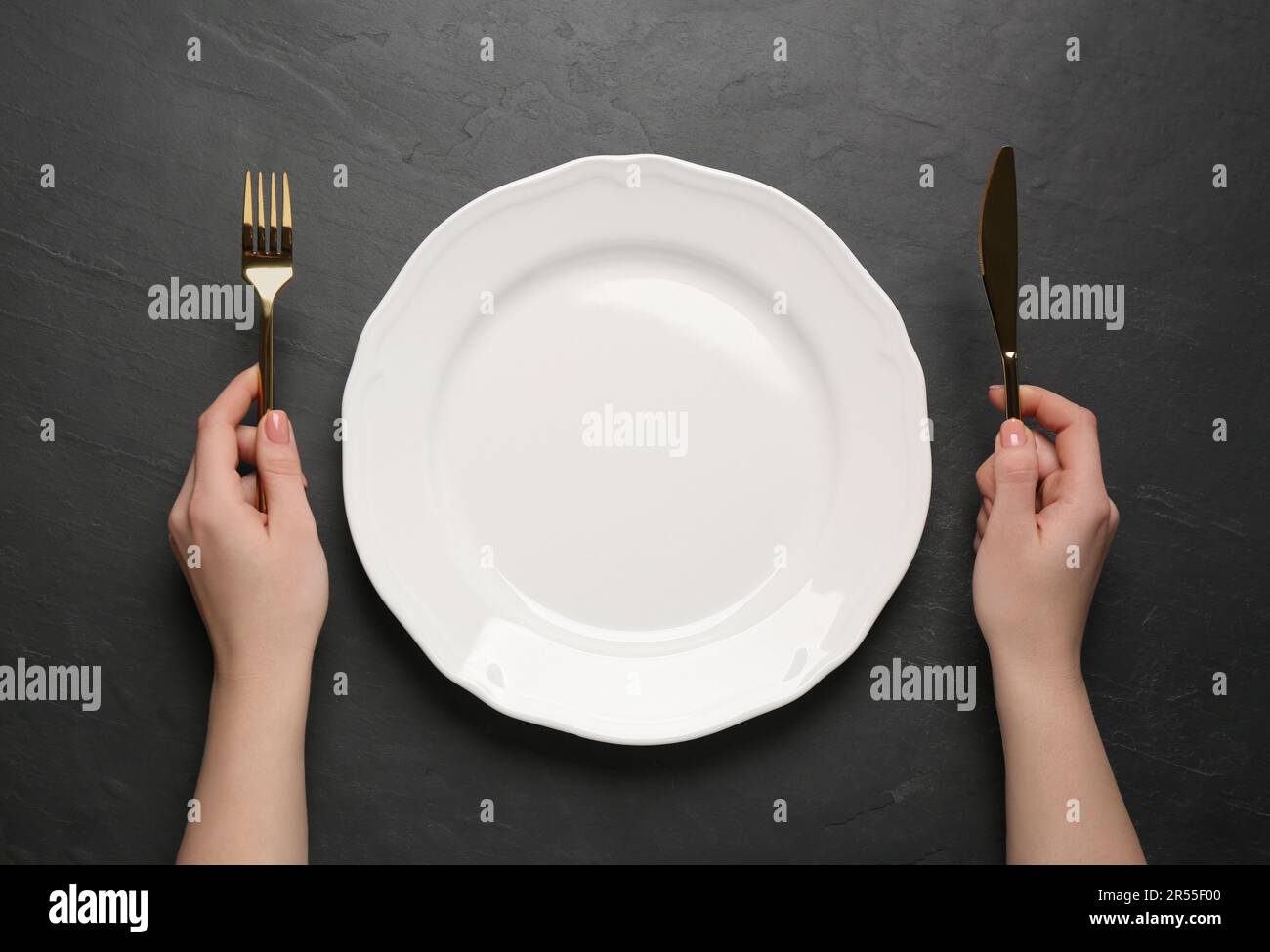 Woman with empty plate and cutlery at black table, top view Stock Photo ...