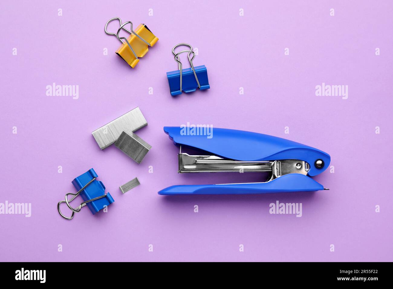 New bright stapler with staples and blinder clips on violet background ...