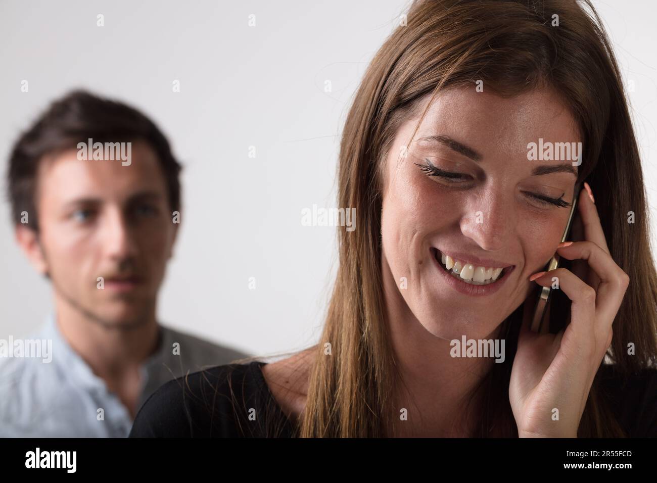 In focus, a woman is engaged on a smartphone call; a suspicious and ...