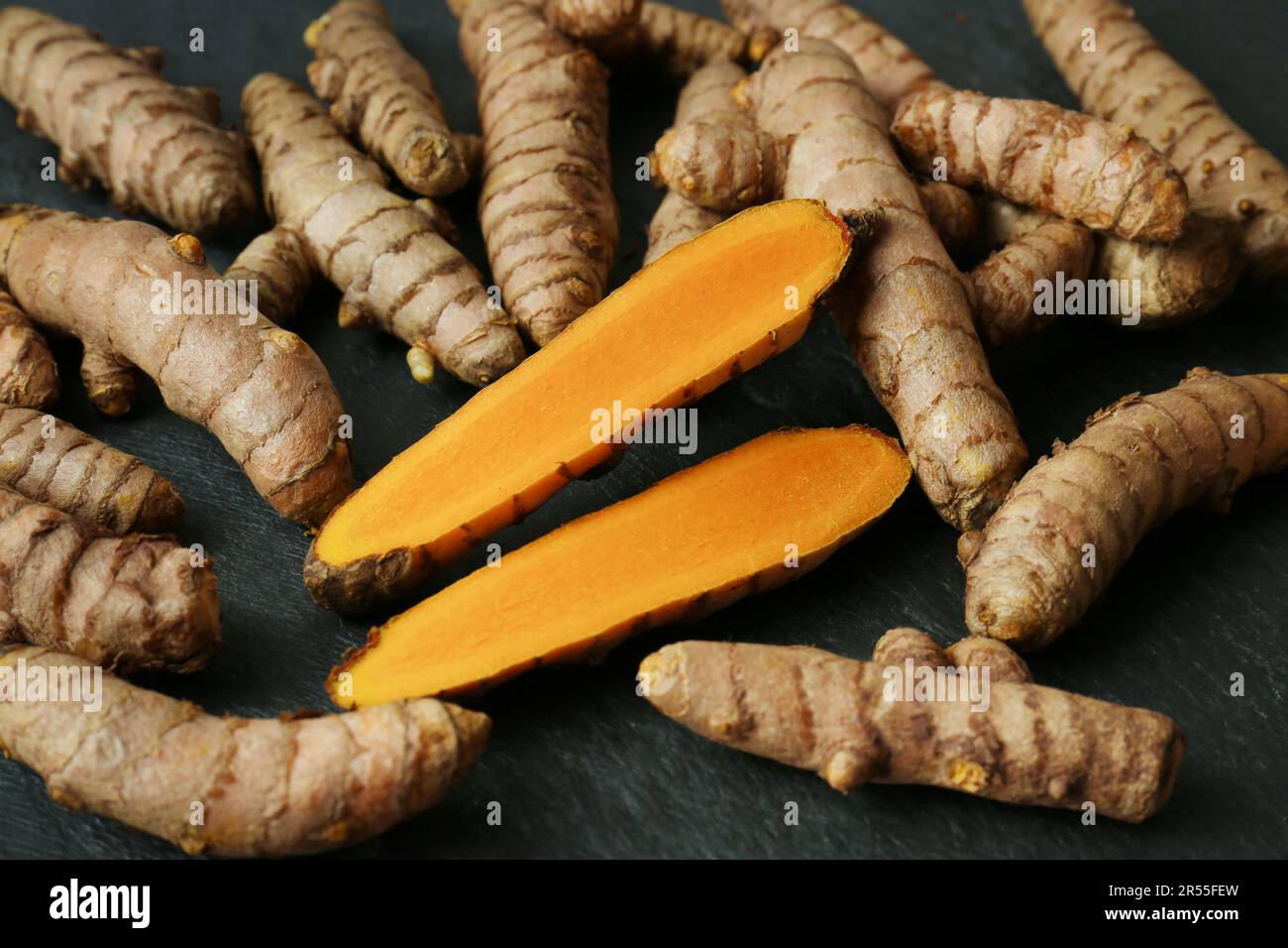 Whole and cut turmeric roots on black textured table, closeup Stock ...