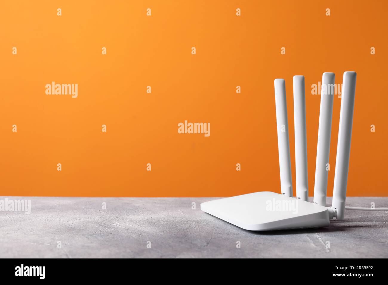 New modern Wi-Fi router on grey table near orange wall, space for text ...