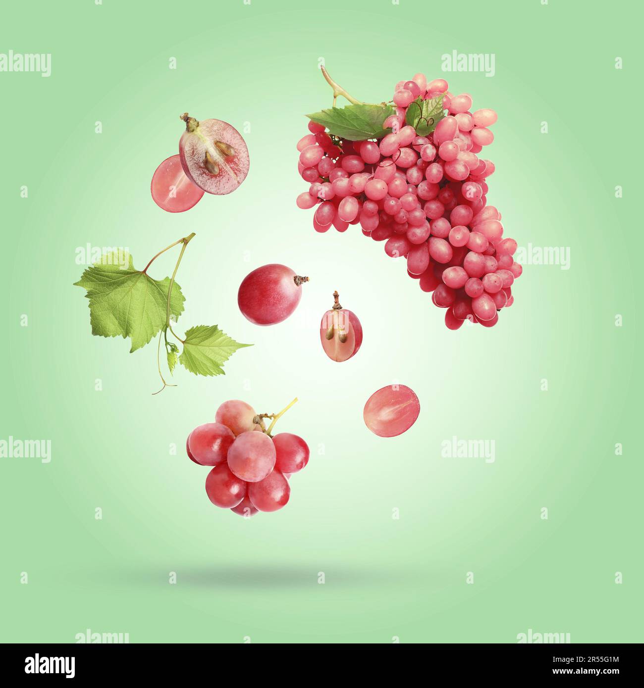 Delicious fresh red grapes and leaves falling on light green background ...