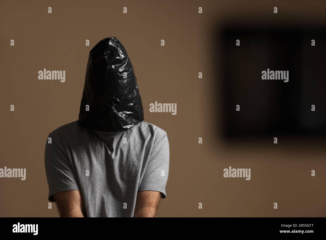 Man wrapped in black plastic bag on his head against dark background ...
