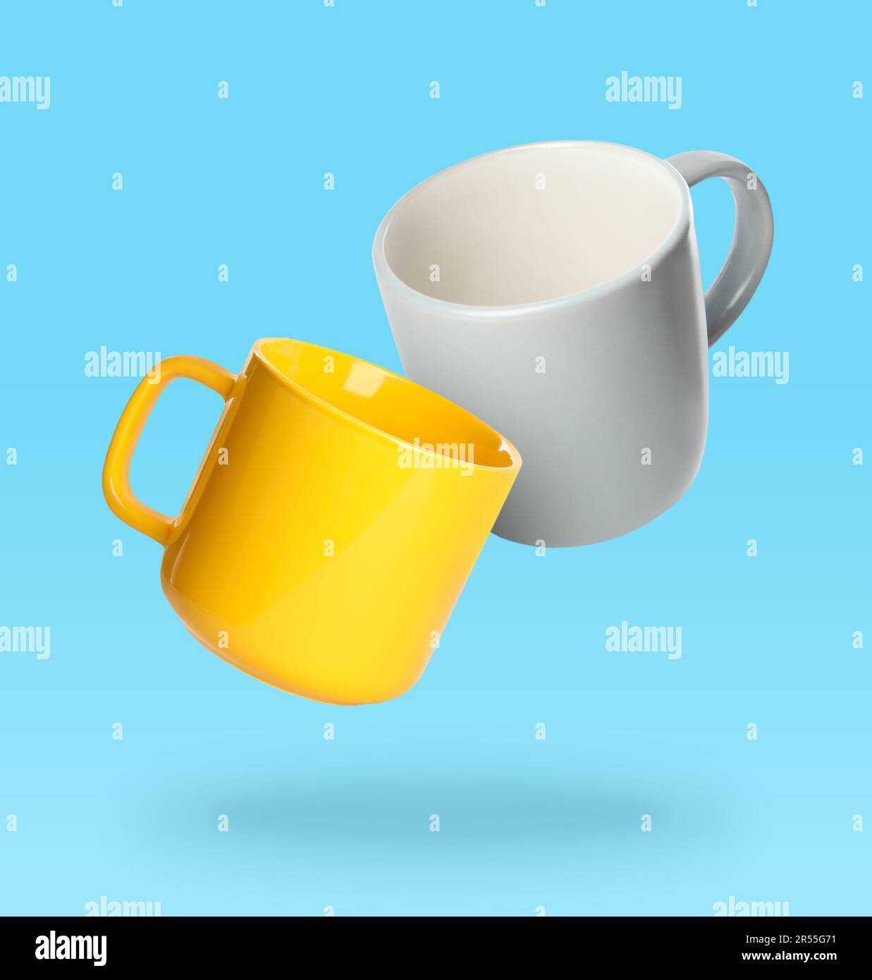 Empty ceramic cups in different colors falling on light blue background ...
