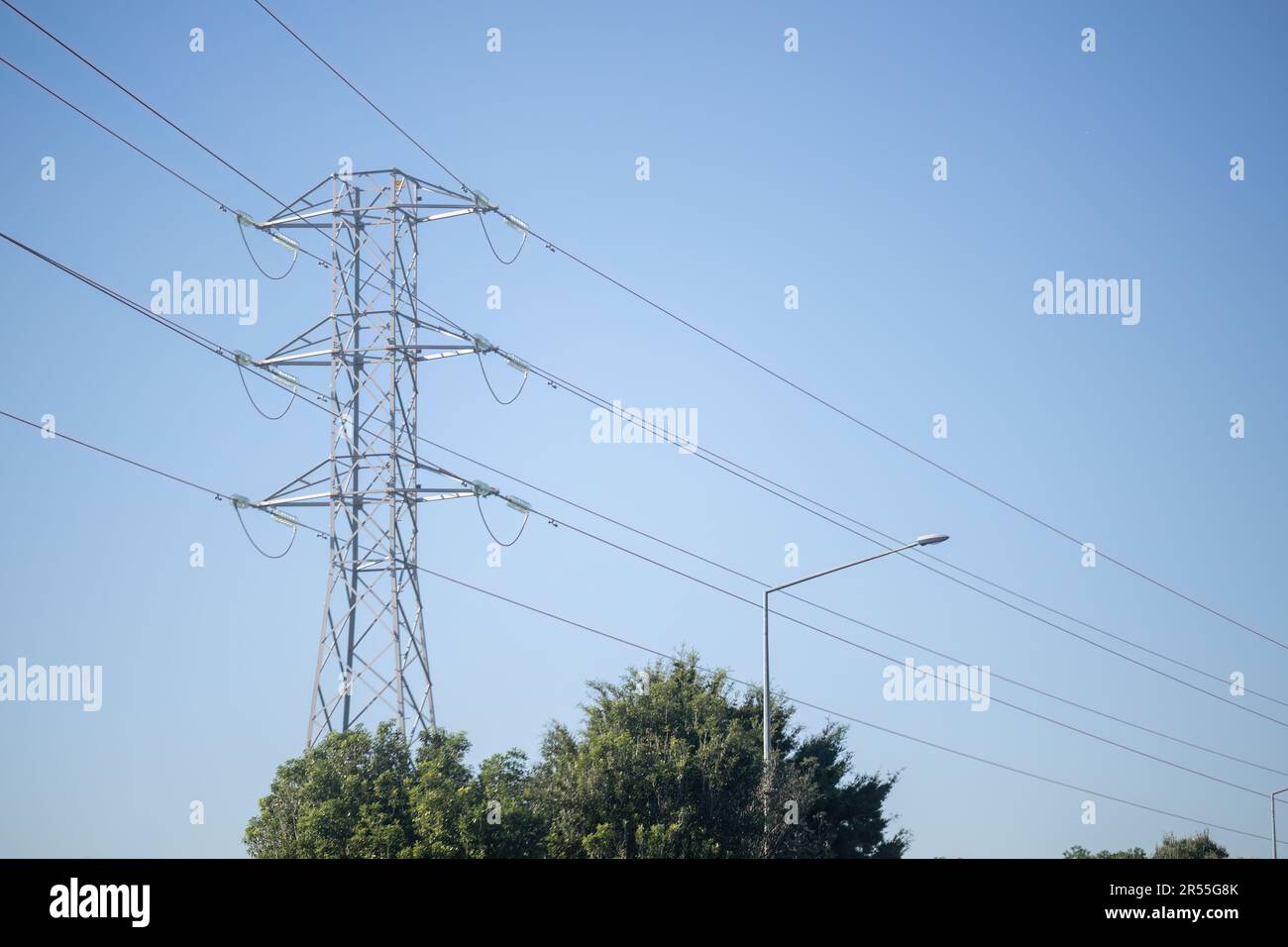 Power pylons and powerlines along the motorway against a clear blue sky ...
