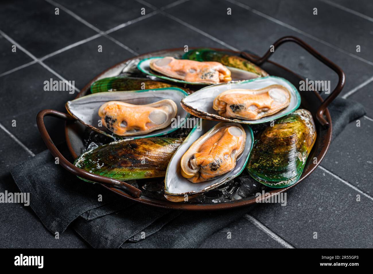 Large green mussels in shells on tray with ice. Black background. Top ...