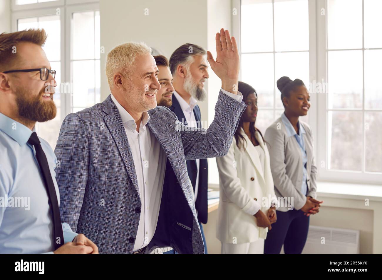 Portrait of a smiling mature business man on a meeting raising his hand ...