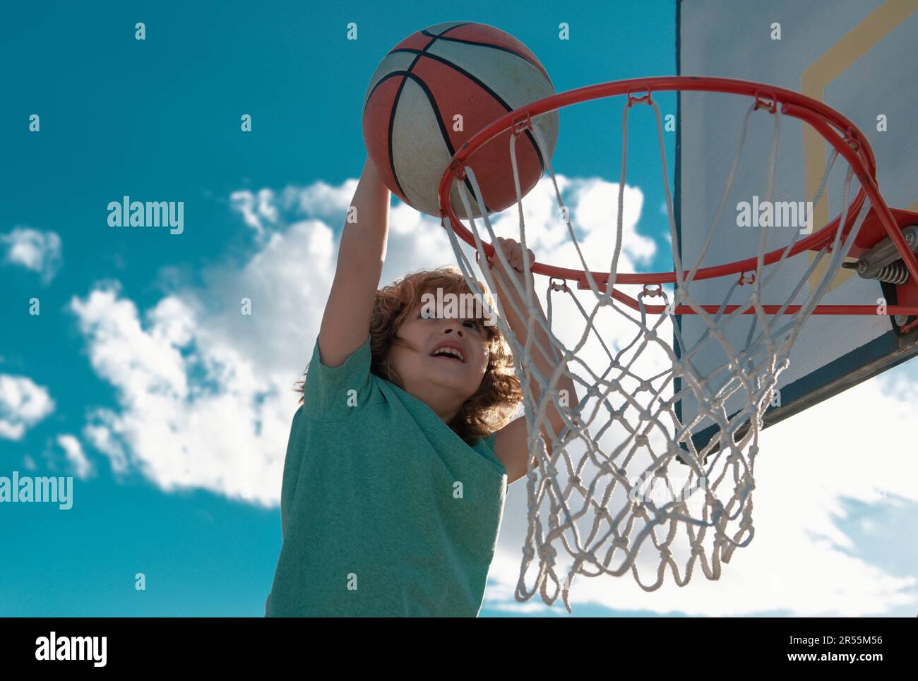 Kid basketball player making slam dunk in blue sky background. The ...