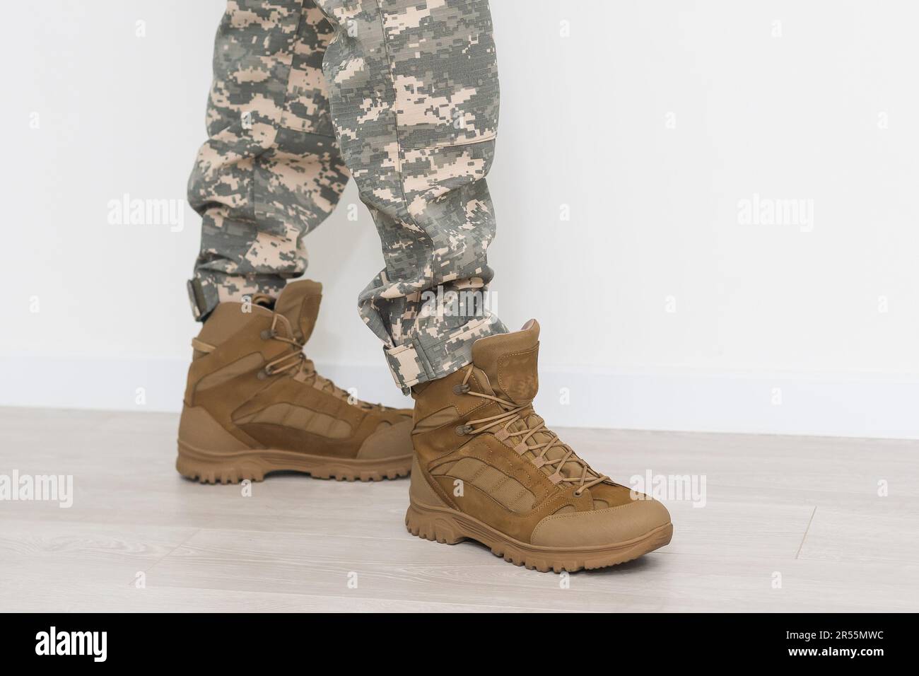 Legs of a soldier in camouflage and army boots on a gray background. Military conflicts and ...