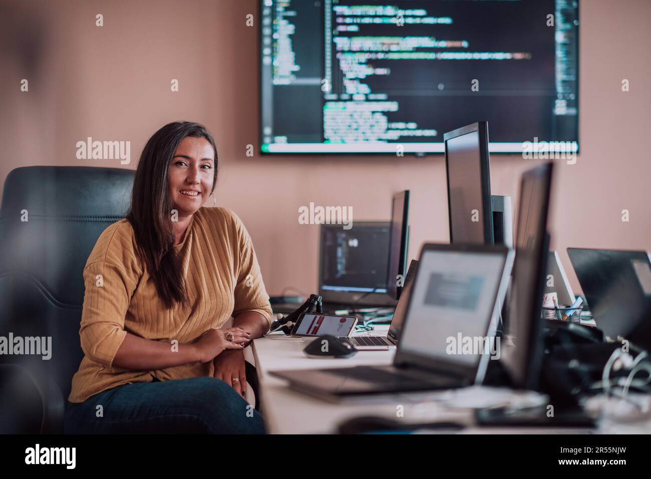 A businesswoman sitting in a programmer's office surrounded by computers, showing her expertise ...
