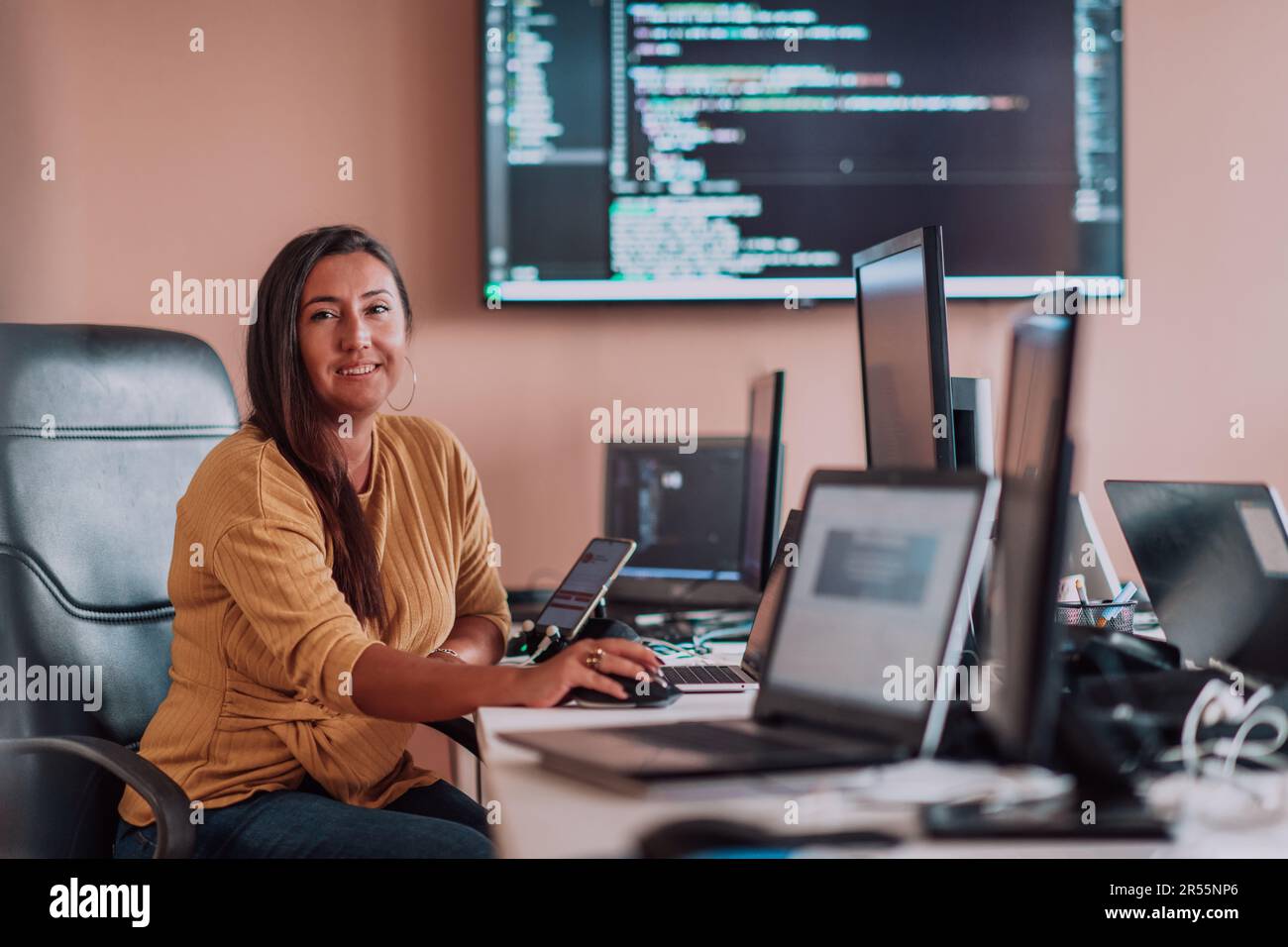 A businesswoman sitting in a programmer's office surrounded by computers, showing her expertise ...