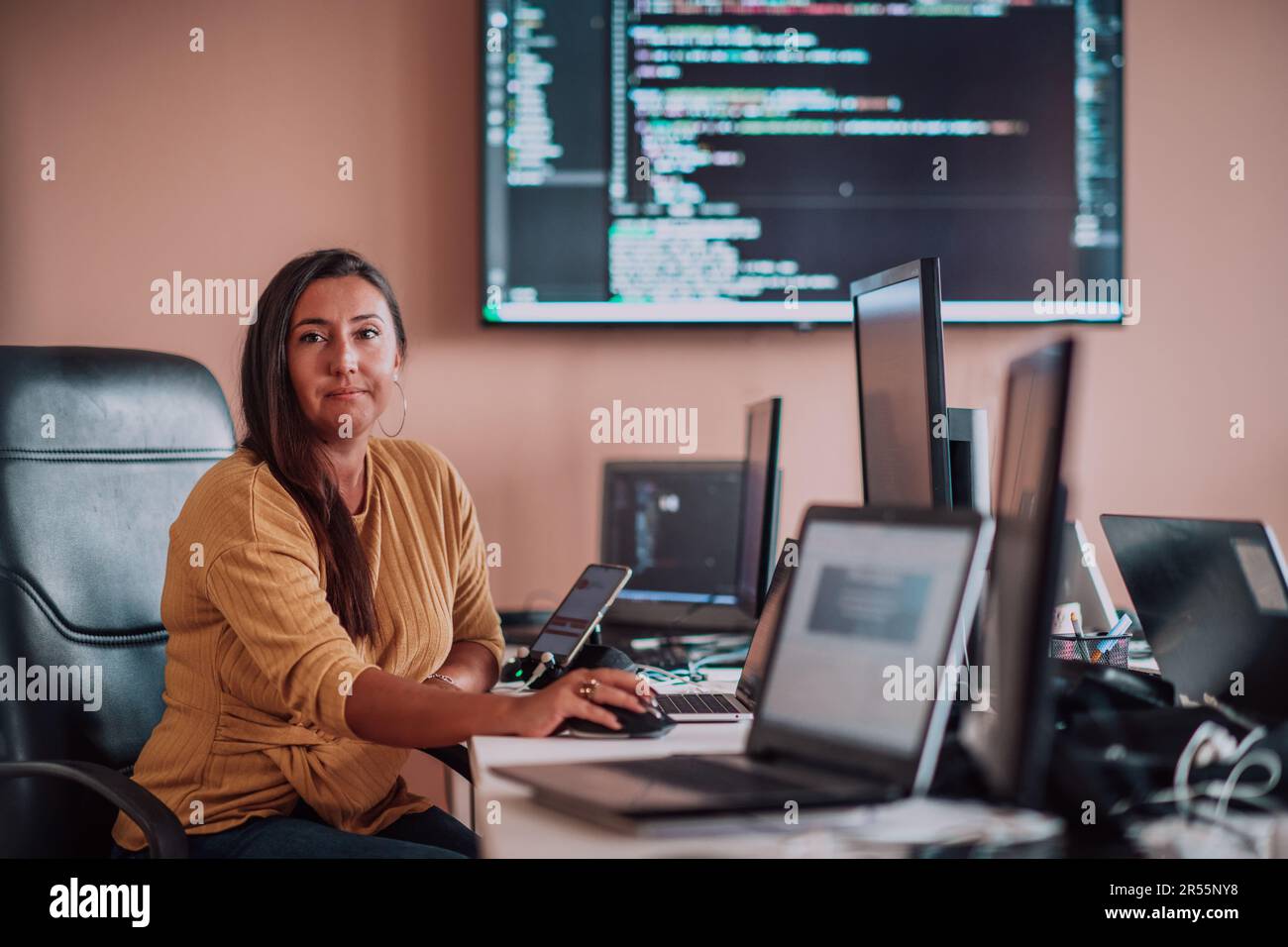 A businesswoman sitting in a programmer's office surrounded by computers, showing her expertise ...