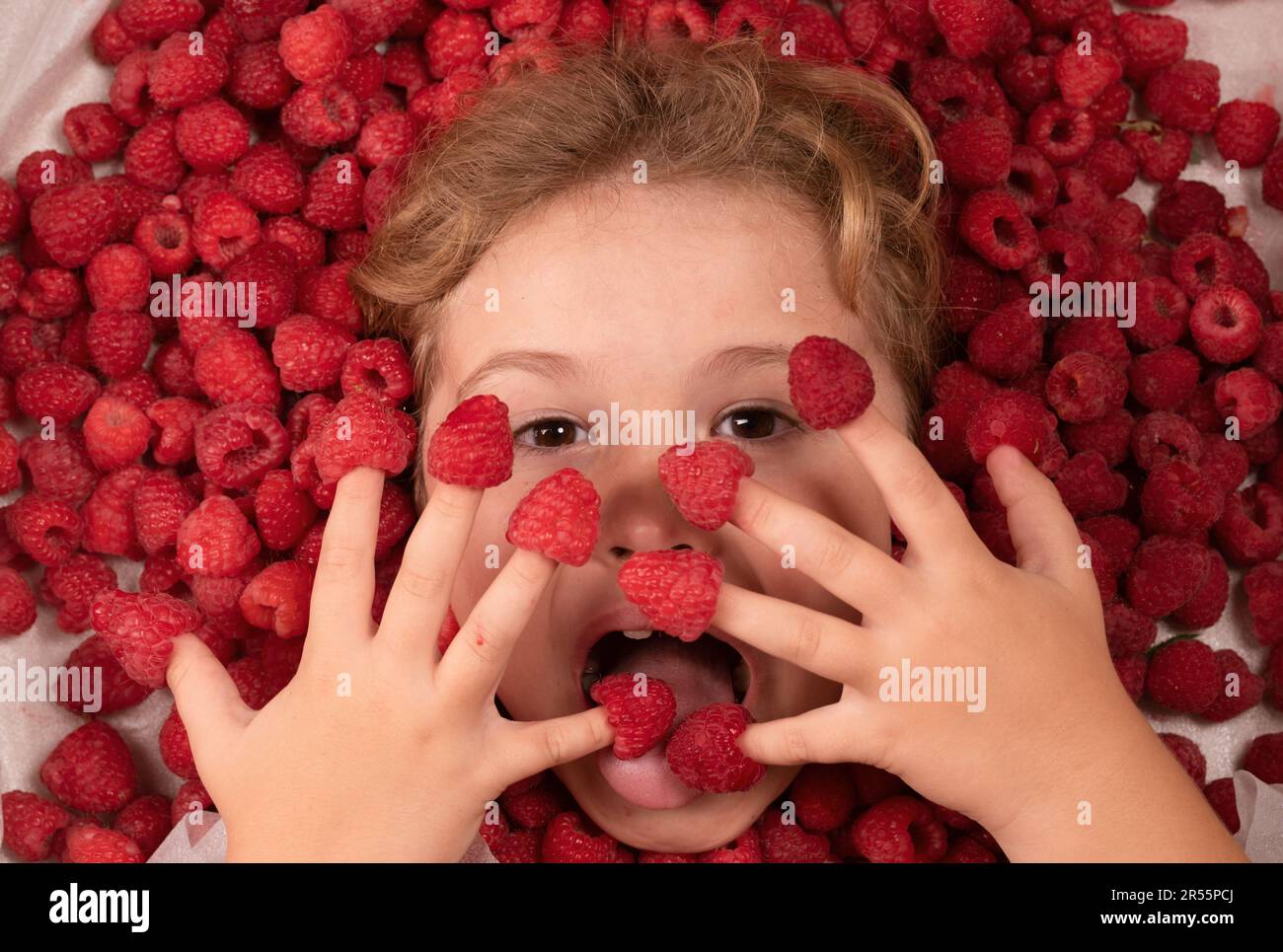 Funny kids face near raspberry background. Cute child eats raspberries ...