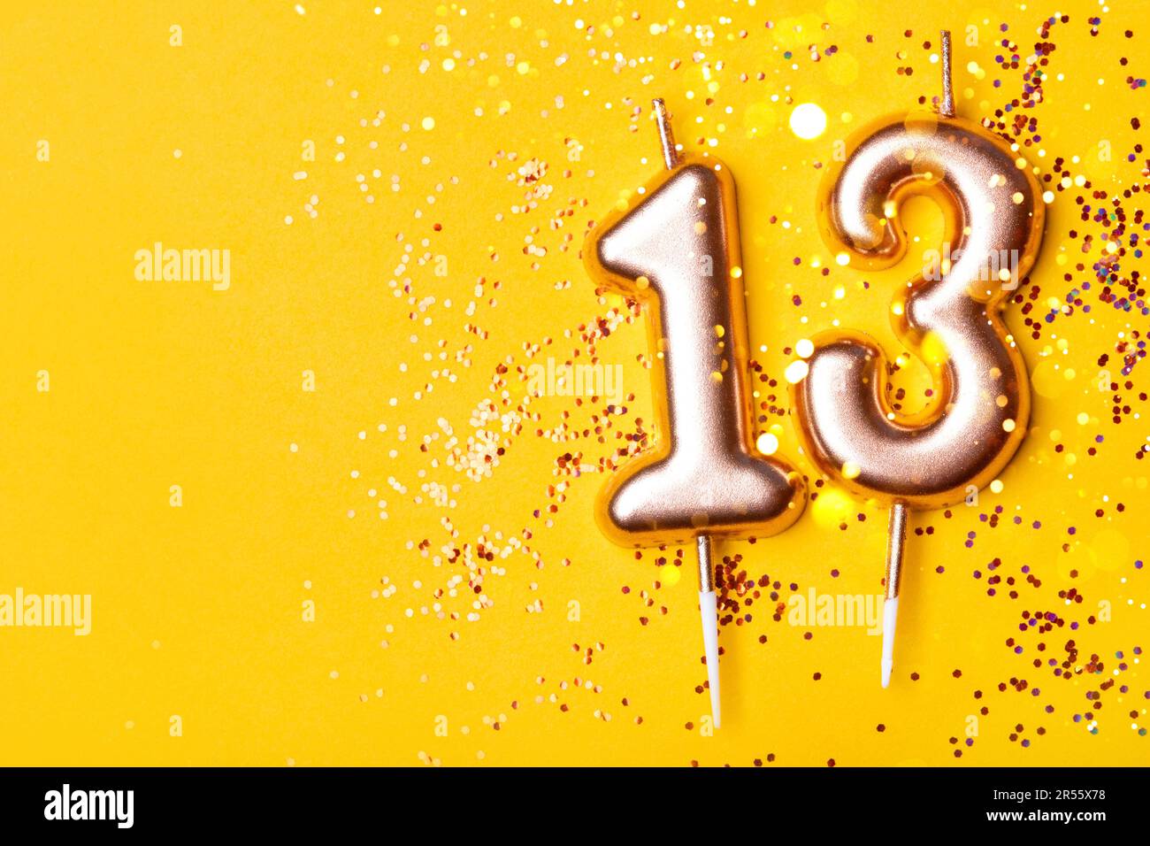 Gold candles in the form of number thirteen on yellow background with ...