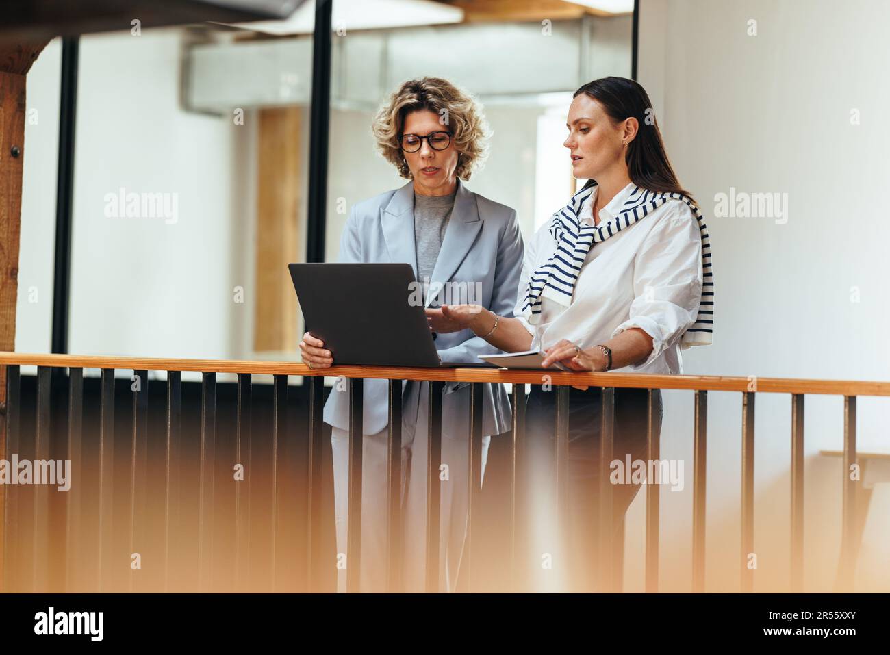 Two business women discuss with each other while using a laptop ...