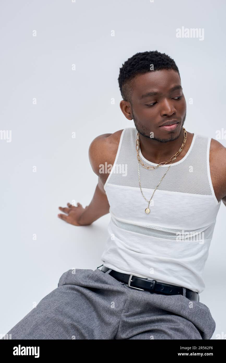 Good looking and young afroamerican man in tank top and pants sitting ...