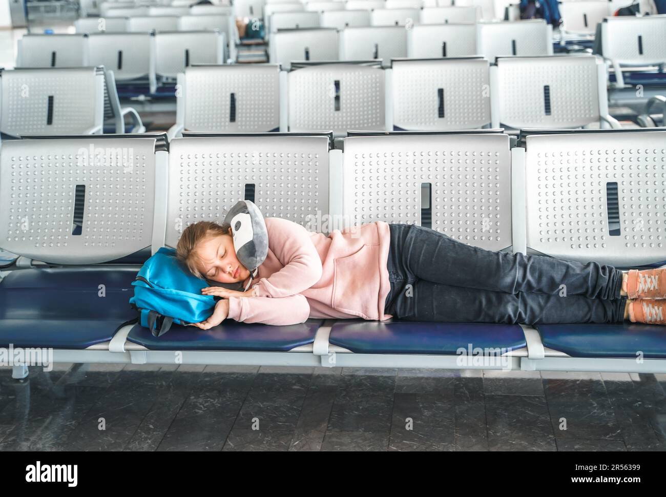 Kid, teen tired girl sleeping, waiting in airport passenger terminal departure hall with ...