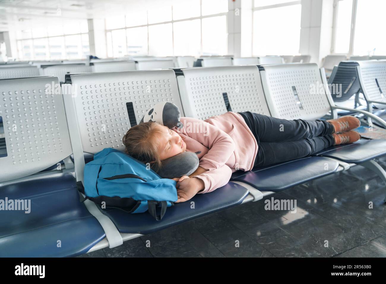Kid, teen tired girl sleeping, waiting in airport passenger terminal departure hall with ...