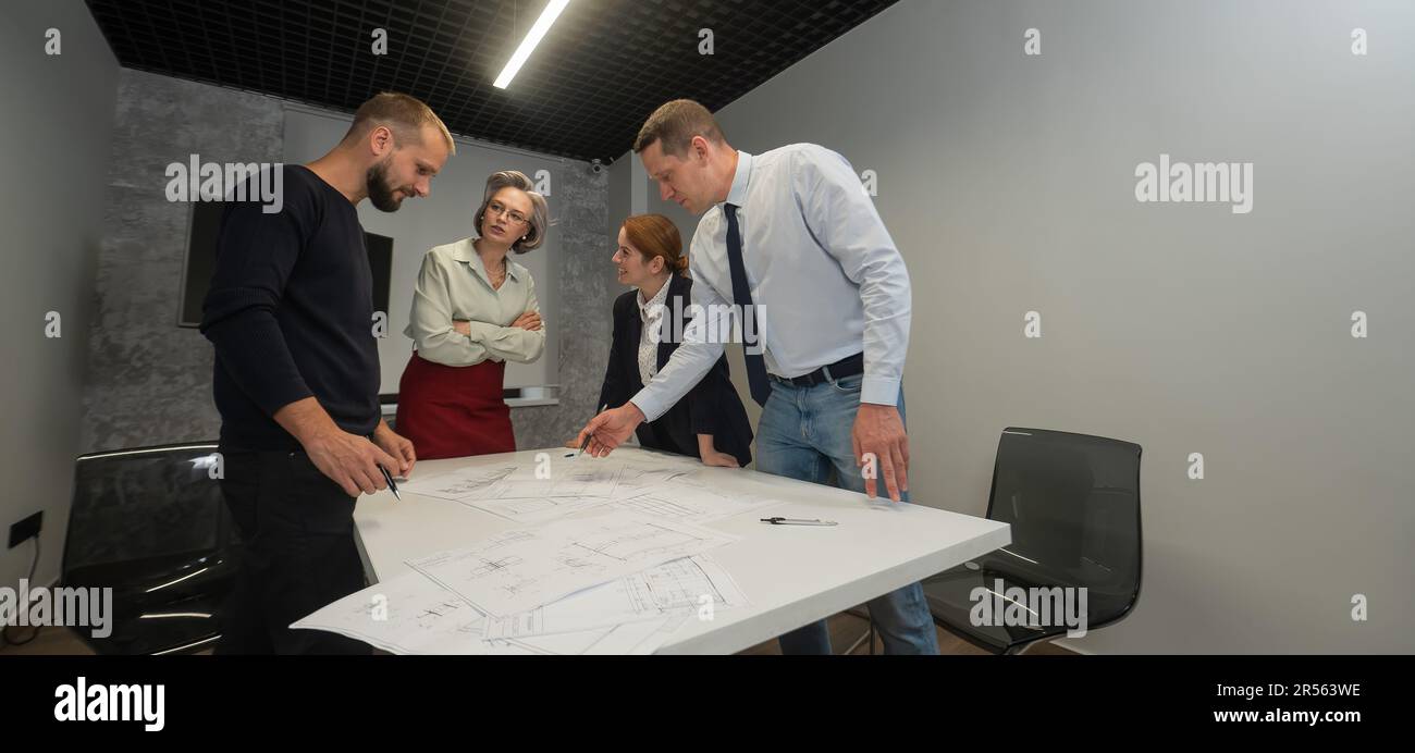 Four business people review and discuss blueprints. Designers engineers ...